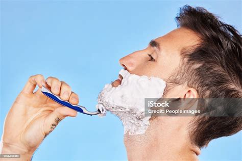 면도 크림 및 남자는 건강 스킨 케어 및 위생을 위해 스튜디오에서 면도기로 수염을 손질합니다 거품 면도기 및 모델은 파란색 배경으로 격리된 얼굴이나 피부 루틴을 위해 수염을