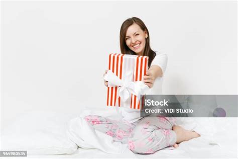 빨간 줄무늬 선물 상자 흰색 시트 베개 담요 흰색 배경에 고립에 배치와 함께 침대에 앉아 젊은 갈색 머리 여자 행복 한 여자 방에 있는 시간을 보내는입니다 나머지 좋은