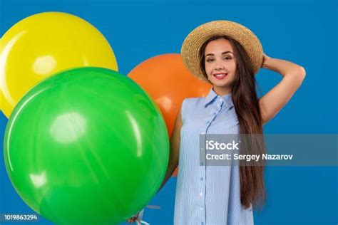 오렌지 노랑 녹색 풍선을 들고 스튜디오에 귀여운 갈색 머리 서 그녀는 밝은 파란색 드레스를 착용 하 고 길고 물결 모양 머리카락을가지고 갈색 머리에 대한 스톡 사진 및 기타