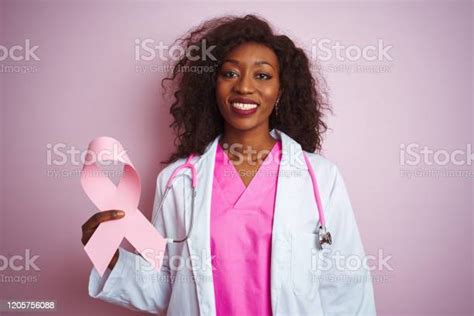 행복한 얼굴 서서 치아를 보여주는 자신감 미소와 함께 미소와 고립 된 분홍색 배경 위에 암 리본을 들고 젊은 아프리카 계 미국인 의사 여자 건강관리와 의술에 대한 스톡 사진