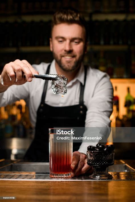 바텐더는 칵테일과 함께 유리 위에 얼음 조각이있는 집게를 들고 있습니다 각얼음에 대한 스톡 사진 및 기타 이미지 각얼음