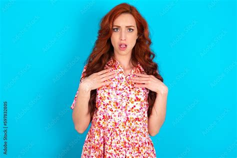 Caucasian Redhead Woman Wearing Floral Dress Over Blue Background Keeps Hands On Chest Feeling