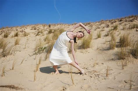 Woman In Flowing White Dress Posing Gracefully On Sandy Dunes Under
