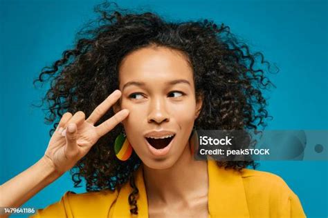 두 손가락으로 승리의 표시를 하고 있는 아프리카계 미국인 여성의 얼굴에 놀란 감정 그녀는 파란색 배경에 자신의 행복을 믿을 수