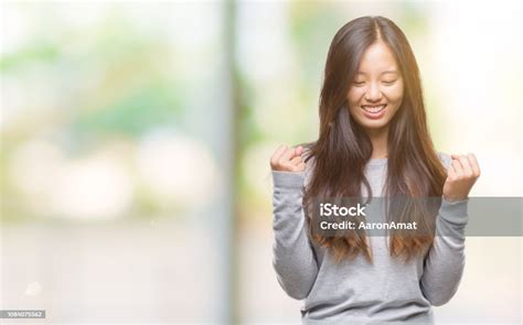 젊은 아시아 여자 격리 된 배경에 매우 행복 하 고 흥분 무기와 우승자 제스처를 하 고 웃 고 성공을 위한 비명 축 하 개념입니다 긍정적인 감정 표현에 대한 스톡 사진 및