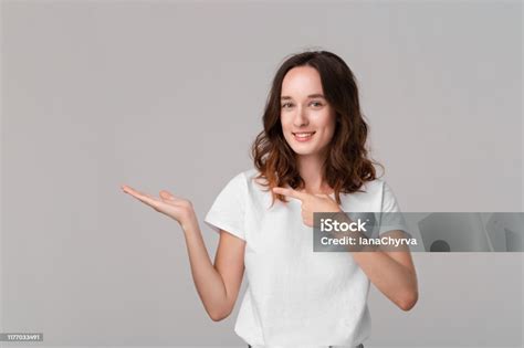 회색 배경 위에 고립 된 제품 배치를위한 빈 공간이있는 손바닥을 들고흰색 티에 예쁜 갈색 머리 여자 광고 의 공간을 복사합니다 T 셔츠에 대한 스톡 사진 및 기타 이미지