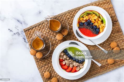 2 신선한 슬라이스 과일 밀 밀기 울 콘플레이크와 코코넛 칩 Chia의 종자 및 열매 건강 한 아침 식사는 시리얼과 딸기와 키 위에서 다른 스무디와 그릇 슈퍼 푸드와 커피