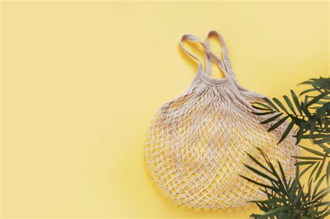 빈 재사용 가능한 쇼핑 문자열 가방과 노란색 배경에 녹색 가지 야자수 잎 제로 폐기물 환경 친화적 인 메쉬 백 플랫 레이 상단