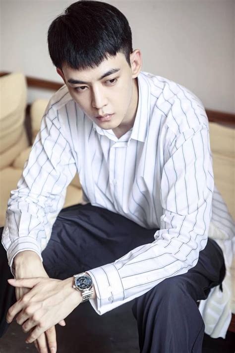 A Young Man Sitting On Top Of A Bed Wearing A White Shirt And Black Pants