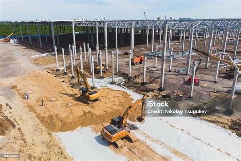 대형 창고 창고 건물 및 물류 센터 건설 현장 중장비 작업 굴삭기 크레인 트럭 및 불도저 현대 공장 격납고의 철골 구조 조감도