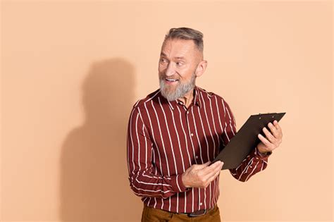 클립보드를 들고 줄무늬 셔츠를 입고 베이지색 배경에 서 있는 자신감 넘치는 고위 사업가 60 64세에 대한 스톡 사진 및 기타