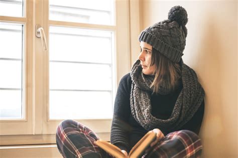 추운 겨울에는 울 모자와 스카프를 들고 책을 읽는 어린 아름다운 소녀 여자는 창 근처에 앉아 있다 집에서 휴식을 취하는 여성 라이프 스타일 잠금 평온과 교육 개념 45 49