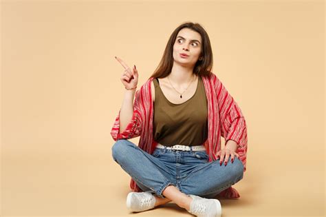 캐주얼 옷에 놀란 된 젊은 여자의 초상화 옆에 앉아 가리키는 인덱스 손가락이 스튜디오에서 파스텔 베이 지 벽 배경에 고립 사람들은 진심으로 감정 라이프 스타일 개념입니다