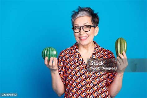 쾌활한 분위기와 다채로운 기발한 패션을 포용하는 생생한 파란색 배경에 장식용 선인장을 들고 있는 쾌활한 선임 여성 50 54세에 대한 스톡 사진 및 기타 이미지 Istock