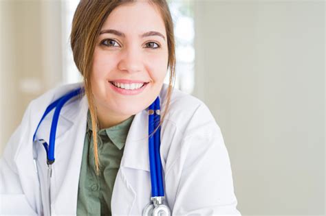 얼굴에 행복하고 시원한 미소와 의료 코트와 청진기를 입고 아름다운 젊은 의사 여성 운이 좋은 사람 건강관리와 의술에 대한 스톡