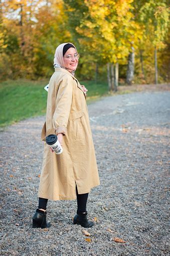 베이지색 트렌치코트를 입은 무슬림 여성이 공원에서 커피 한 잔과 노트북을 들고 서 있다 비즈니스 메모장 무슬림 비즈니스 우먼 학생 20 24세에 대한 스톡 사진 및 기타