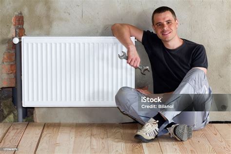 새로 지어진 아파트 또는 집의 빈 방에 성공적으로 설치 난방 라디에이터 근처 손에 렌치와 바닥에 앉아 젊은 잘 생긴 배관공 건설 유지 보수 및 수리 개념 가정의 방에 대한