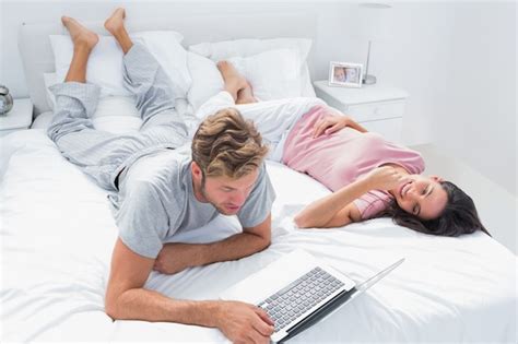 Premium Photo Man Using A Laptop Next To His Wife Lying On Bed