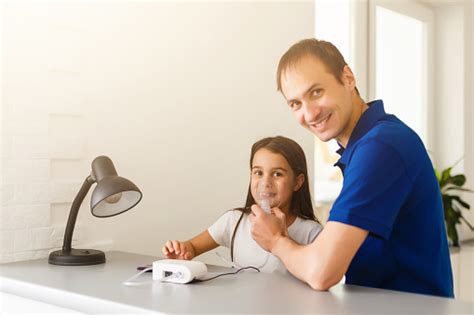 집에서 분무기로 흡입하는 어린 유아 소녀 아버지가 장치를 돕고 들고 계십니다 독감 기침 및 기관지염을 가진 아이 천식 흡입기 흡입 증기 아픈 개념 2명에 대한 스톡 사진 및