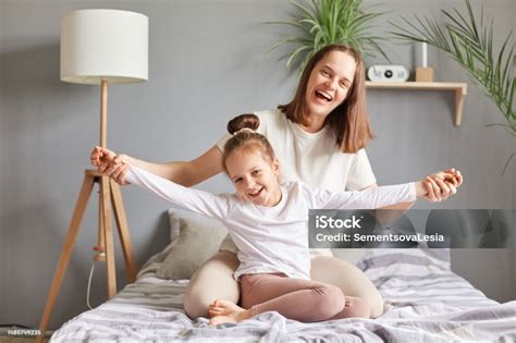 어머니와 딸은 집에서 즐거운 시간을 보내고 있다 어머니의 날을 축하하는 엄마와 아이 침실에 앉아 있습니다 날아가는 것처럼 팔을 벌리고 있습니다 행복 표현 2명에 대한 스톡