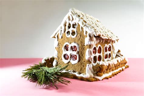 흰색 달콤한 아이싱으로 칠해진 홈메이드 진저브레드 하우스는 흰색과 분홍색 배경에 녹색 소나무 가지로 장식되어 있습니다 건축물에 대한 스톡 사진 및 기타 이미지 Istock