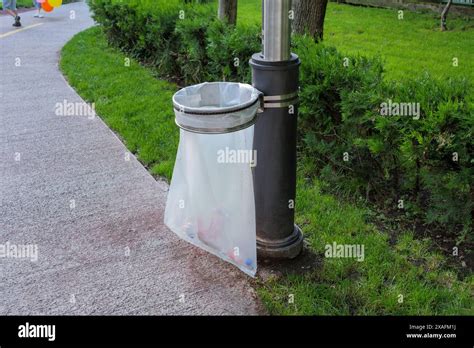 A Plastic Trash Bag With Garbage Inside Is Attached To A Lamppost Along