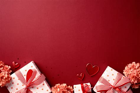 하트 패턴의 종이와 빨간 리본으로 싸인 선물 상자가 있는 발렌타인 데이 컨셉 빨간 배경에 분홍색 꽃과 하트 모양의 장식으로 둘러싸여 있습니다 로맨틱한 축하 행사에 딱