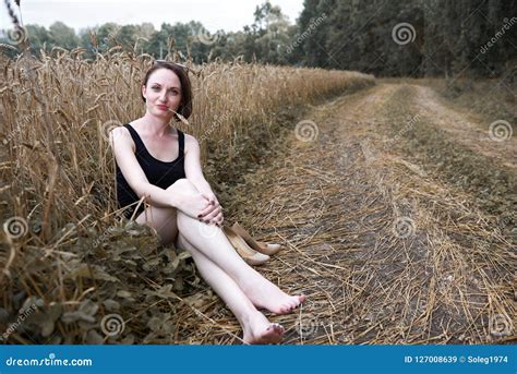 Young Girl Sitting Barefoot On The Ground Road Near Wheaten Field Concept Of Summer And Travel