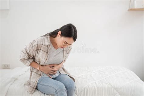 A Woman With Pain In Her Stomach Is Sitting On The Bed At Home Stock Photo Image Of Adult