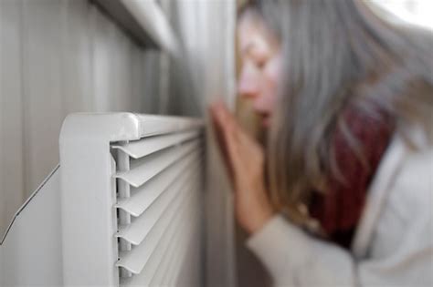 스웨터를 착용 한 젊은 냉동 여성은 얼굴에 충격적인 표정으로 겨울 추위를 위해 흔들리고 얼어 붙습니다 소녀는 전기 히터 위에 숨을 쉬며 손을 데우고 있습니다 집에서 시간을