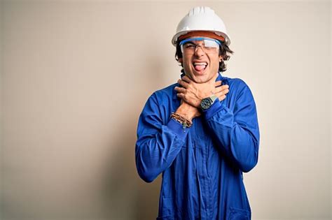 고립 된 흰색 배경 위에 유니폼과 보안 헬멧을 착용한 젊은 생성자 남자가 고통스러운 목졸림 때문에 외치고 질식합니다 건강 문제