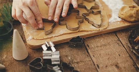 나무 보드에 크리스마스 금속 절단기로 진저 브레드 반죽을 손으로 자르고 변덕스러운 이미지 향신료 장식 롤링 핀으로 소박한 테이블에 전통적인 크리스마스 진저 브레드