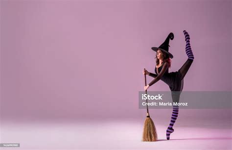모자에 검은 마녀 의상을 입고 빗자루를 입은 뾰족한 신발에 발레리나가 라일락 배경의 지붕에서 춤을 추고 있습니다 할로윈에 대한 스톡 사진 및 기타 이미지 Istock