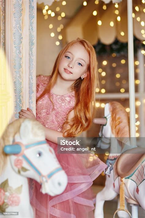 긴 머리와 파란 눈을 가진 아름 다운 빨간 머리 소녀 긴 핑크 드레스에 회전 목마를 타고 말의 형태로 회전 목마 놀이 공원에서 그녀의 생일을 축 하는 빨강 머리 소녀 고풍