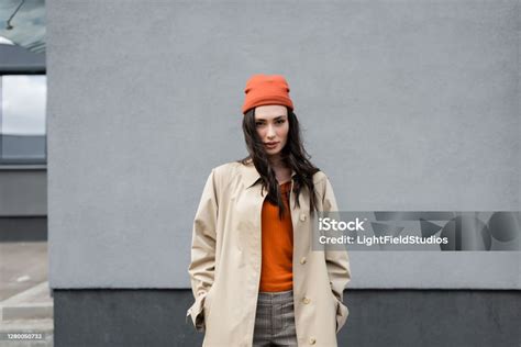 트렌치코트와 비니 모자를 입은 세련된 여성 건물 근처 주머니에 손을 얹고 서 있는 것 트렌치 코트에 대한 스톡 사진 및 기타 이미지 트렌치 코트 니트 모자 한 명의