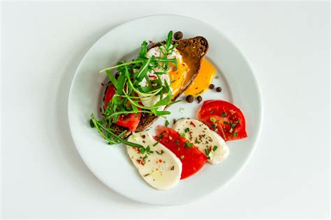 토마토 모짜렐라 아루굴라 향신료 후추를 흰 접시에 얹은 검은 호밀 빵 조각에 맛있는 데친 달걀 갈색 빵에 대한 스톡 사진 및