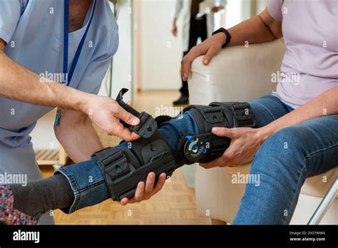 A Male Nurse Helps To Put A Bondage Medical Splint Knee Brace On The Leg Of An Elderly Female