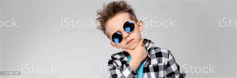 잘생긴 소년 격자 무늬 셔츠 블루 셔츠와 청바지에 회색 배경에 서 있다 소년 라운드 안경 쓰고 있습니다 빨간 머리 소년 그의 턱을 그의 손에 보유 개념에 대한 스톡 사진 및