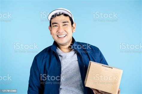 파란 재킷과 모자를 쓰고 배달 서비스에서 행복한 아시아 남자 음식 주문을주고 파란색 배경에 고립 된 상자를 들고 나름에 대한 스톡 사진 및 기타 이미지 Istock