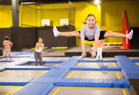 Full Length Of Happy Casual Girl Jumping Spreading Legs On Colorful Trampoline At Playground