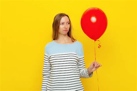 혼란스러운 젊은 여성은 빨간색 팽창 헬륨 풍선을 들고 당혹스럽고 기분을 상하게하며 축하 행사 중에 기분이 좋지 않습니다 휴일과