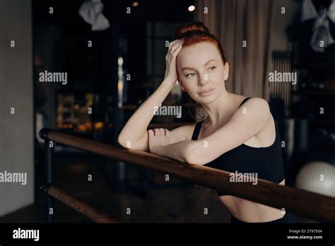 Graceful Redhead In A Ballet Studio Rests At The Barre Embodying Calm And Poise In Her Athletic