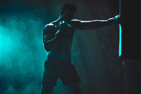 어두운 체육관에서 펀칭 백으로 스파링하는 인식 할 수없는 권투 선수의 실루엣 다가오는 싸움을 준비하기 위해 운동하는 남자 운동 선수 젊은 무술가 훈련 및 연습 20 24세에