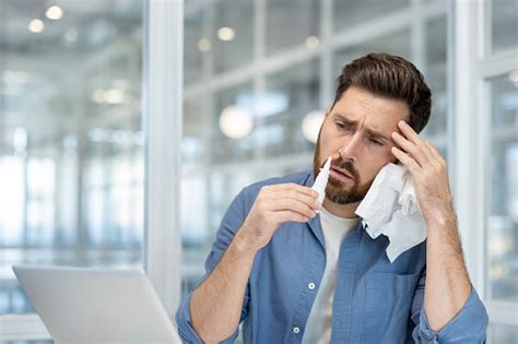 손에 티슈를 들고 비강 스프레이를 뿌린 아픈 직장인 독감과 감기에 걸린 남자가 직장 사무실에 앉아 코를 흘리고 재채기를 합니다 35 39세에 대한 스톡 사진 및 기타 이미지