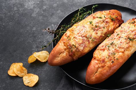 바게트 보트 양피지와 검은 색 어두운 콘크리트 배경에 햄 베이컨 야채 및 치즈가있는 바게트 빵에 뜨거운 구운 샌드위치 상단 보기 공간을 복사합니다 가공육에 대한 스톡 사진