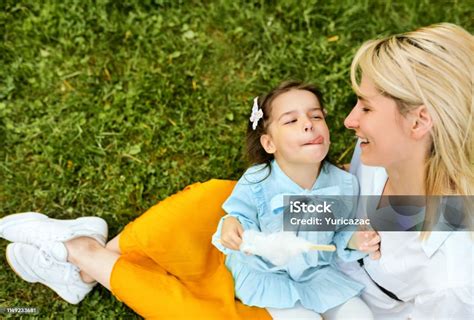 녹색 잔디에 앉아 공원에서 그녀의 젊은 어머니와 함께 솜 사탕을 먹는 아름 다운 딸의 평면도 이미지 아름 다운 여 자가 야외에서