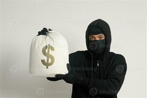 Mysterious Robber Thief Man Wearing Black Hoodie And Mask Carrying A Bag Full Of Money Isolated