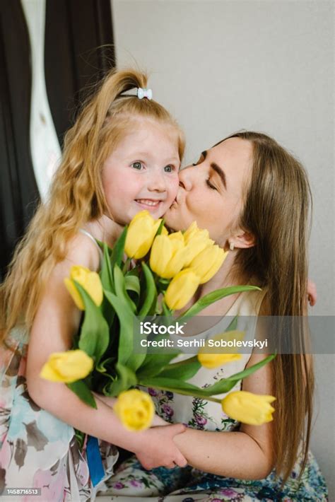 귀여운 소녀가 어머니를 맞이하고 집에서 노란 꽃 튤립 꽃다발을 준다 어머니의 날 개념입니다 엄마와 딸은 웃고 키스합니다 행복한 가족 휴가와 공생 측면도 2명에 대한 스톡