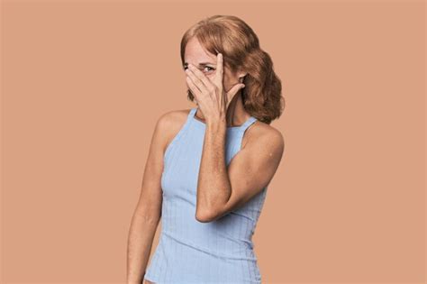 Premium Photo Redhead Midaged Caucasian Woman In Studio Blink At The Camera Through Fingers