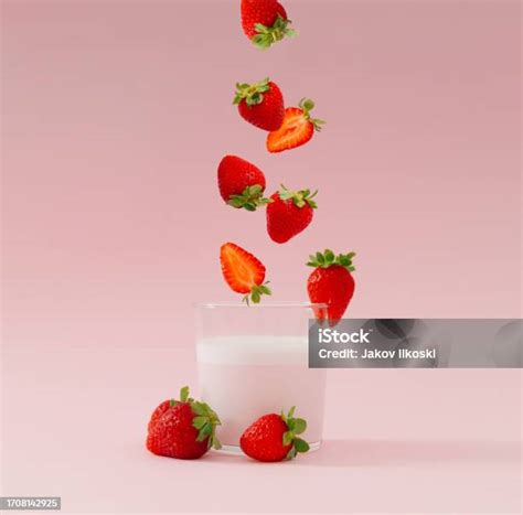 파스텔 핑크 배경에 딸기 맛이 있는 우유 음료의 유리 컵에 떨어지는 딸기로 만든 창의적인 레이아웃 최소한의 스무디 또는 밀크 쉐이크 개념 아침 식사와 간식으로 건강에 좋은